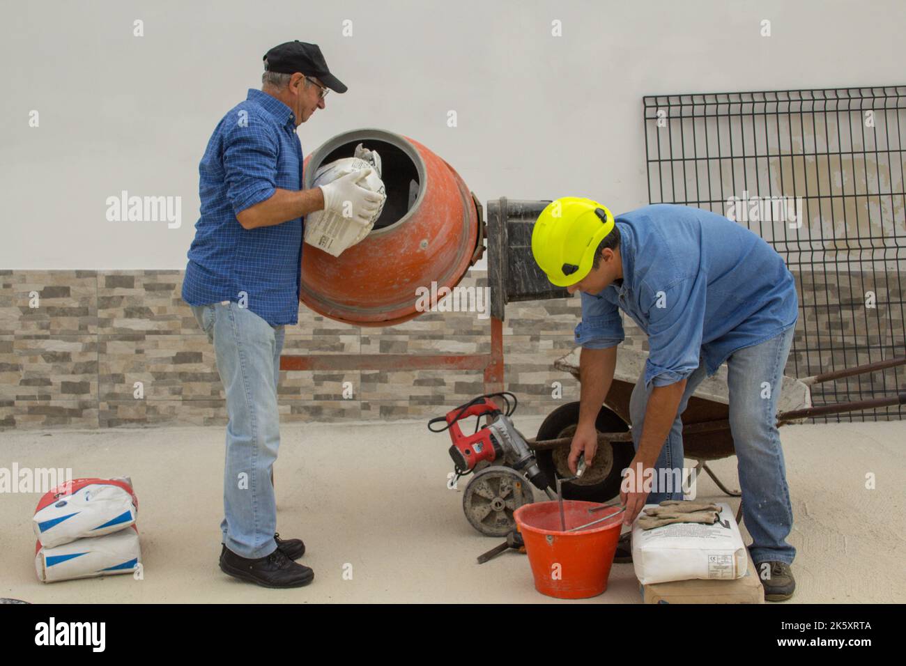 An elderly bricklayer and a young one are mixing concrete with a ...