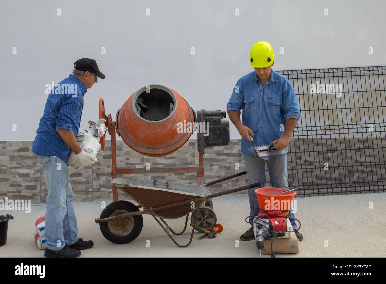 An elderly bricklayer and a young one are mixing concrete with a ...