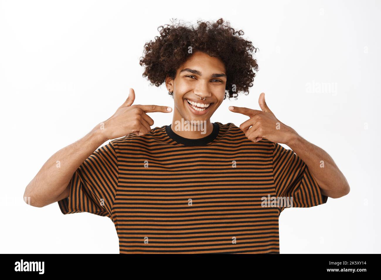 Happy handsome boy with curly hair, pointing at his white teeth ...