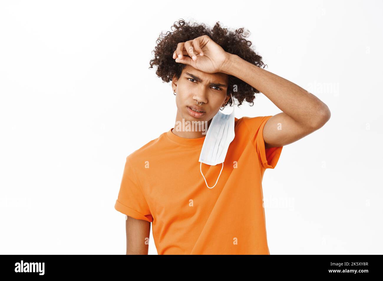 Image of tired hispanic guy takes off medical face mask and wipes sweat ...