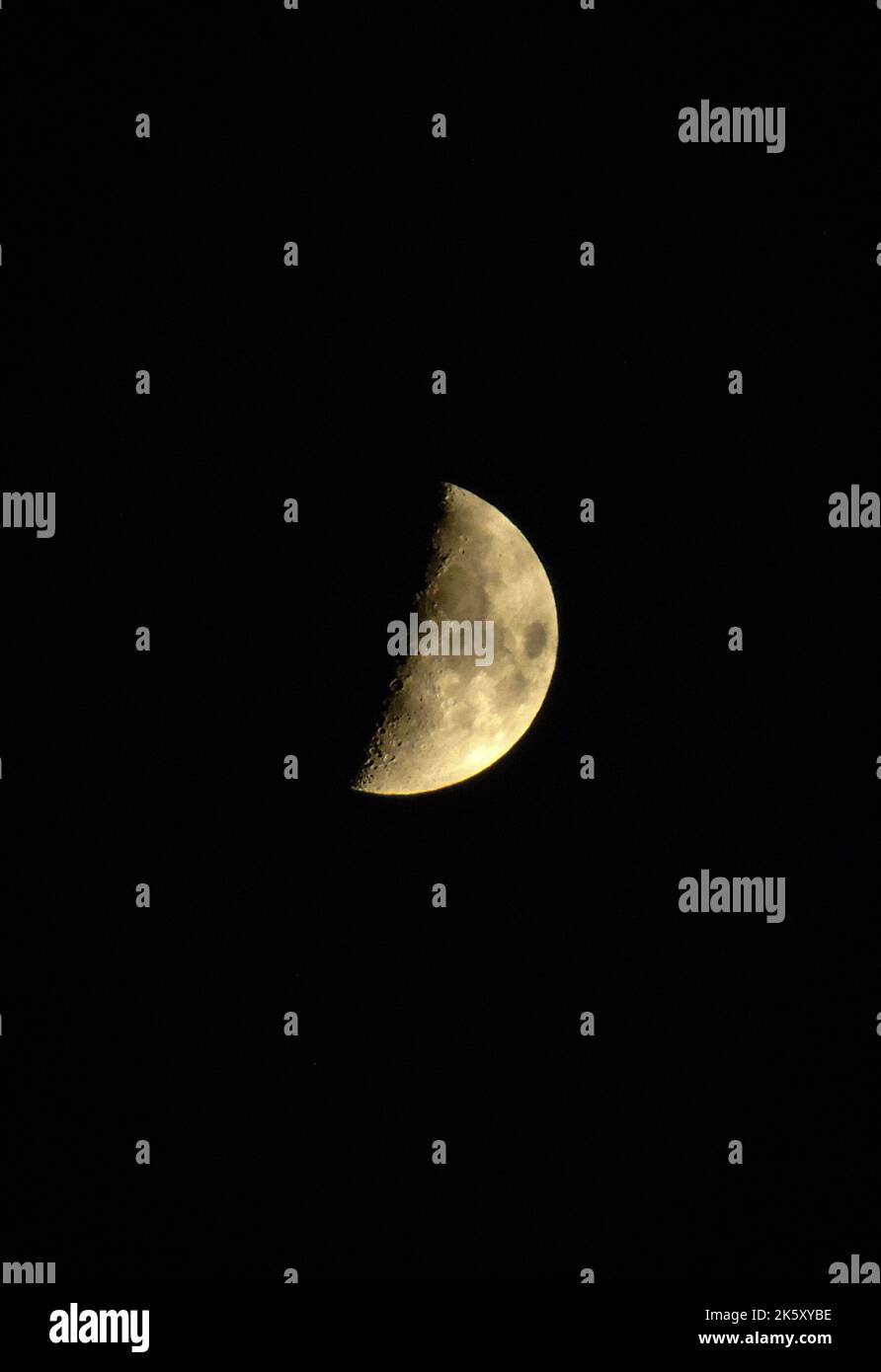 A vertical closeup of a gray half moon with details isolated on black ...