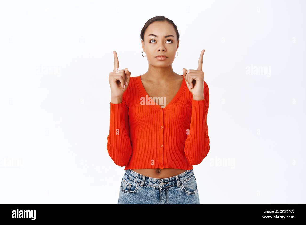 Portrait of young woman looks with doubt and skepticism, pointing ...