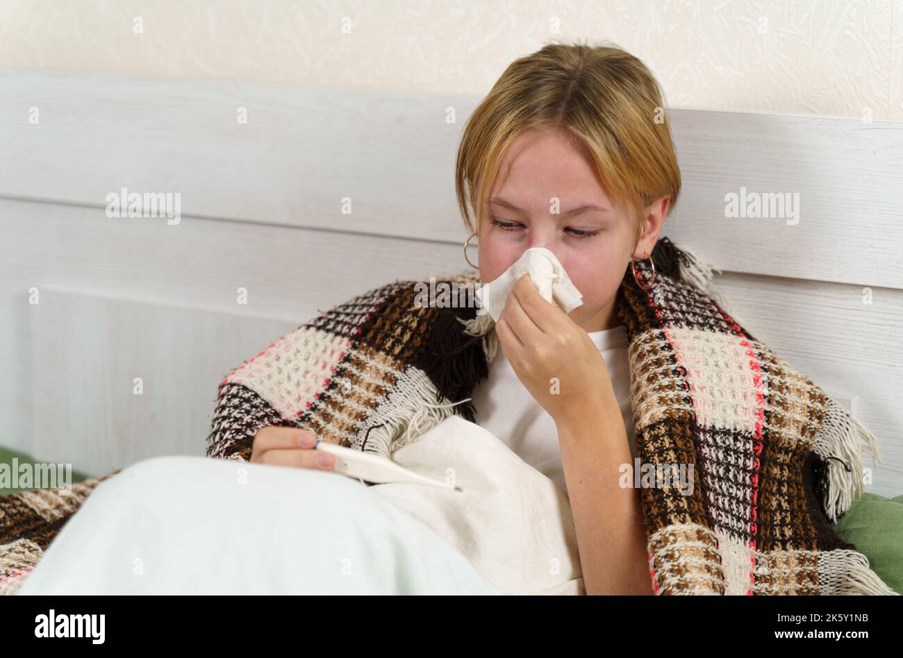 The sick girl wrapped herself in a blanket, looks at the thermometer ...