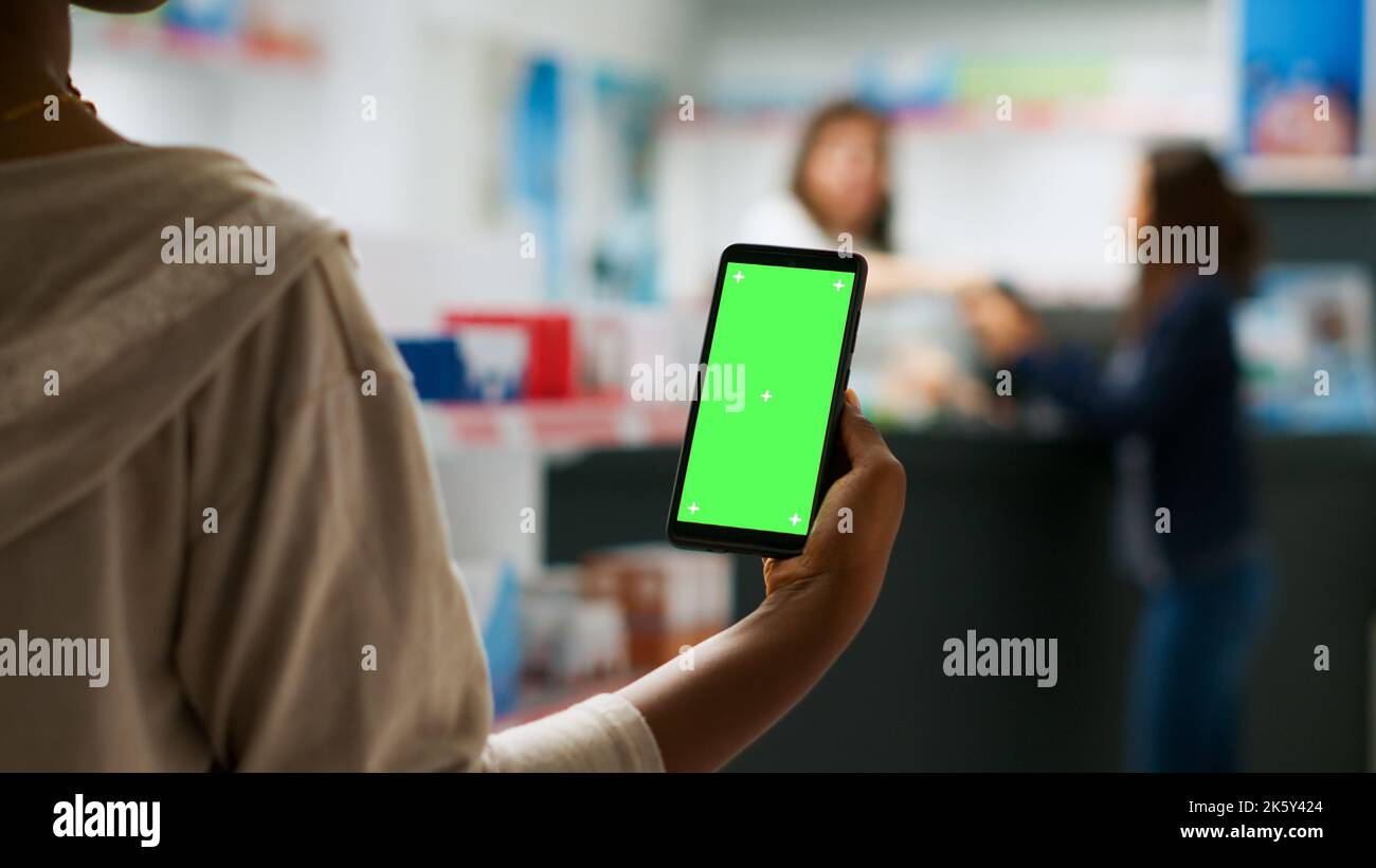 Female client holding smartphone with greenscreen display in pharmacy ...