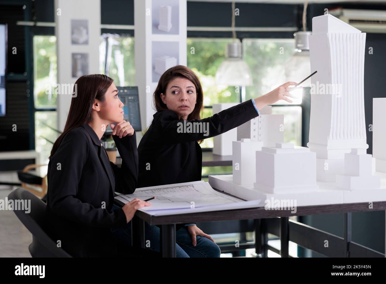 Women working with project draft, discussing building 3d printed model in architecture office ...