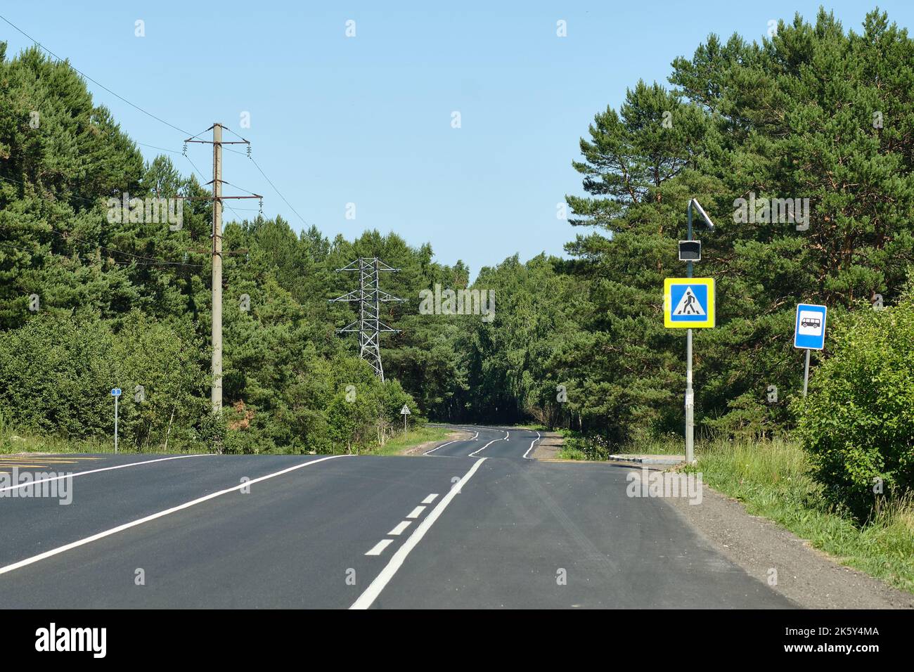 A countryside road surrounded by trees, road signs and powerline poles ...