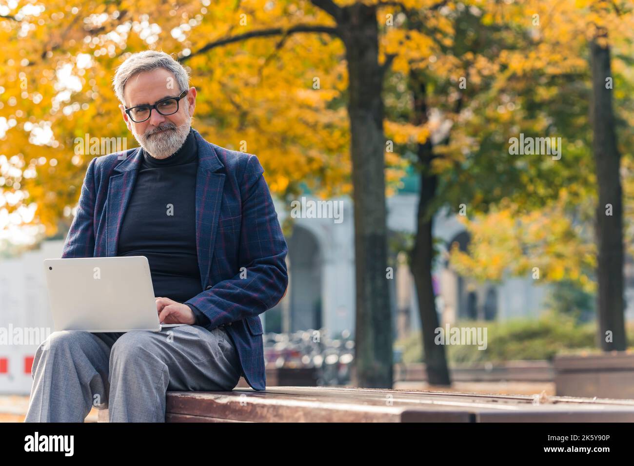 Elegant caucasian gray-haired man working remotely on his white laptop ...