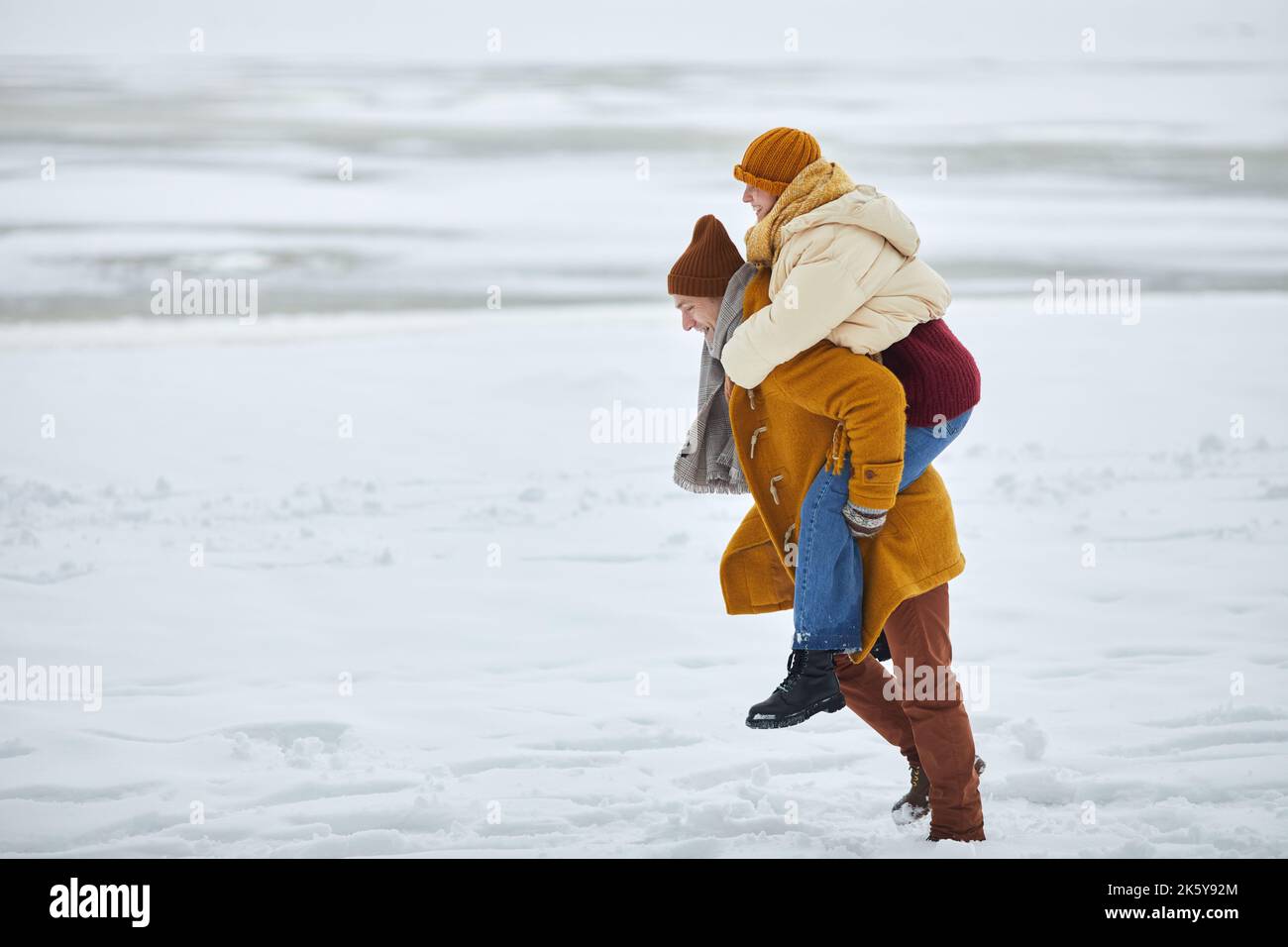 Side view portrait of young man carrying girlfriend on shoulders while ...