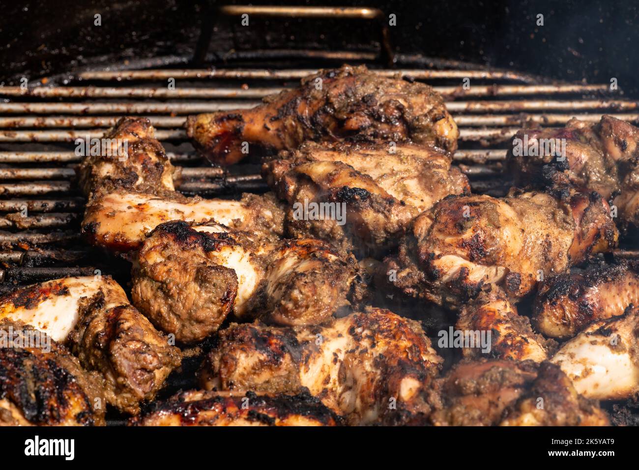 Grilling traditional Jamaican spicy jerk chicken with over charcoal ...