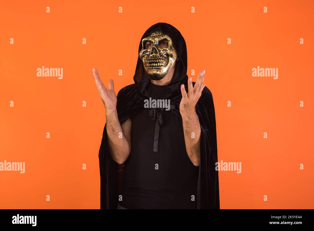 Person with skull mask and black cape with hood, in a praying position ...