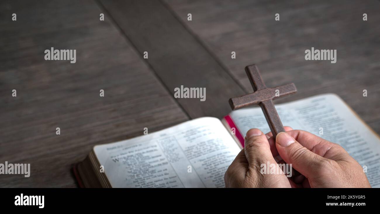 Hand holding religious crucifix cross on top of Holy Bible. Christian ...