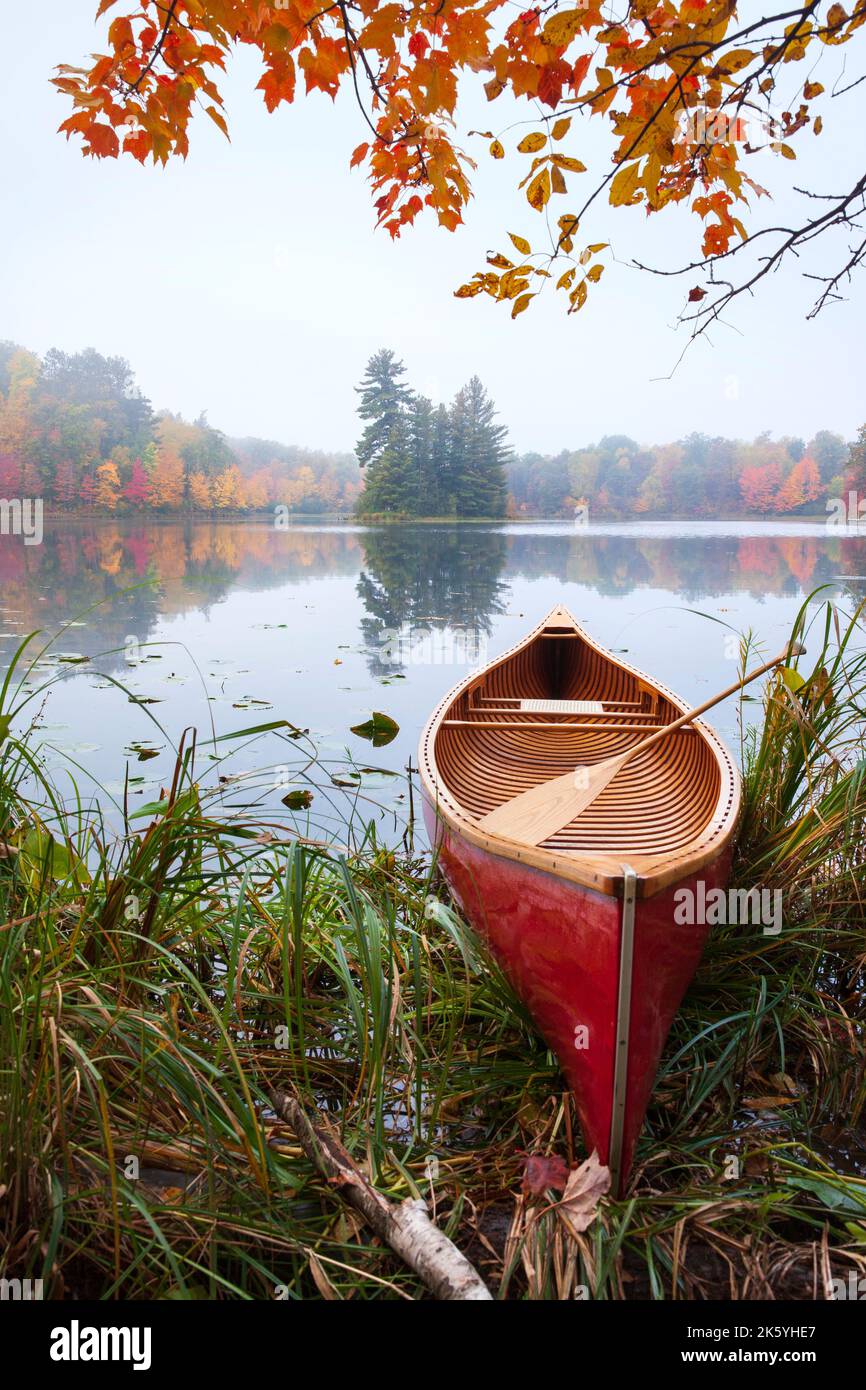 Red wooden canoe on calm lake with trees in fall color and maple ...