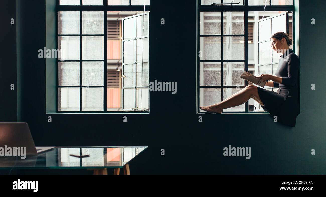 Side view of woman sitting by window and reading a magazine. Young ...