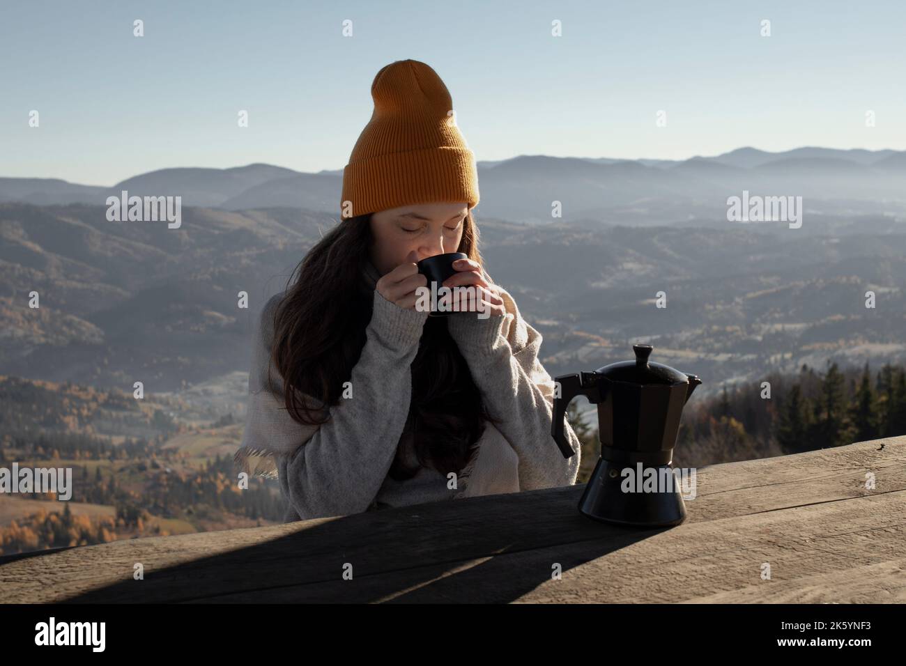 Woman is sitting at wooden table and drinking coffee in front of ...