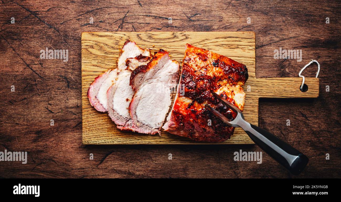 Baked pork loin, whole and cut meat pieces on rustic wooden cutting ...