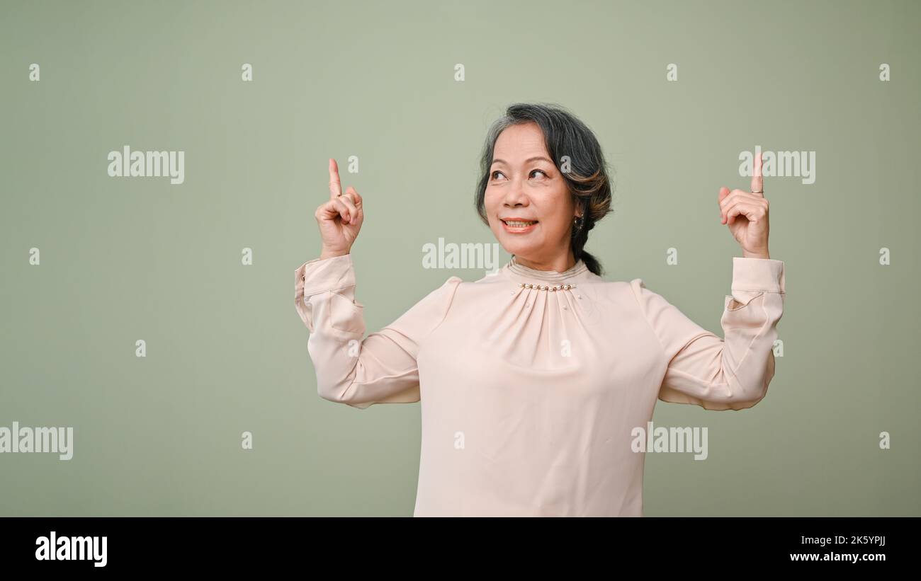 Beautiful and happy 60s aged-asian woman smiling, lifting her fingers ...