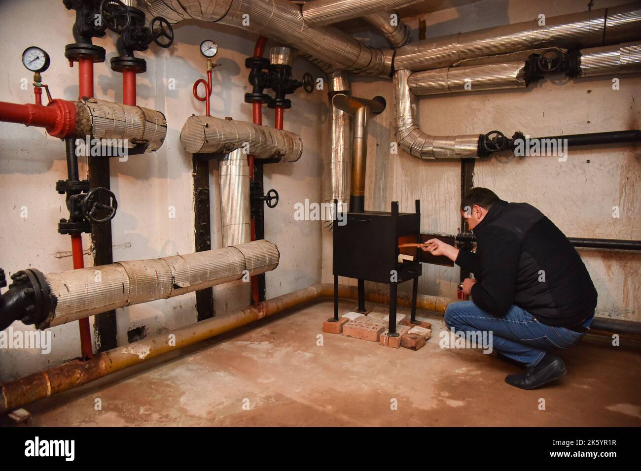 A man lights a metal stove in the basement of a house that serves as a ...