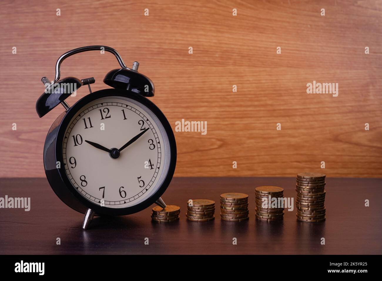 Black alarm clock and stacked golden coin on wooden background Stock ...