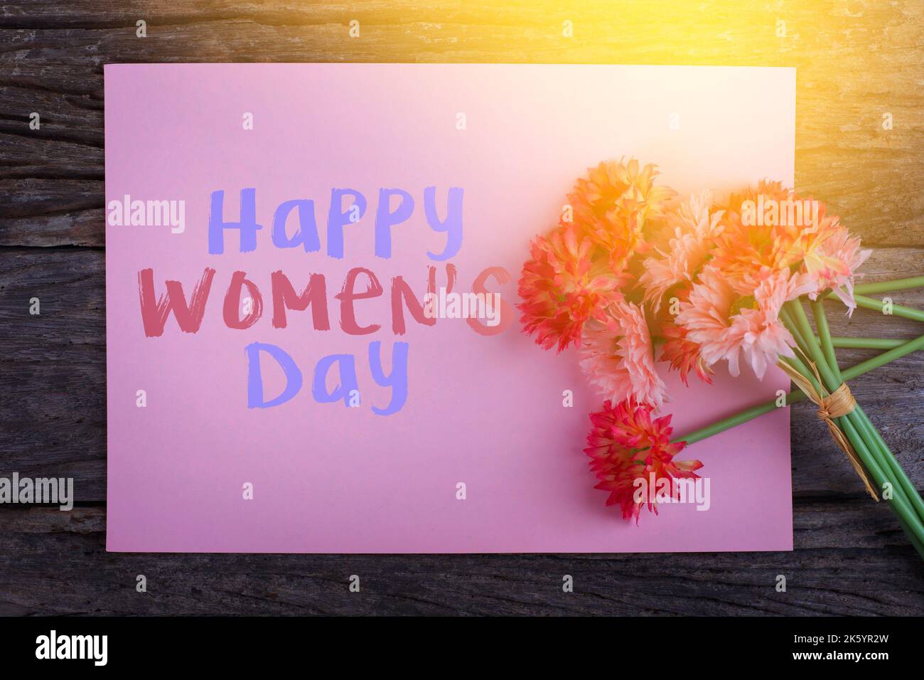 HAPPY WOMENS DAY WRITTEN ON A PIECE OF PAPER WITH PINK FLOWER Stock ...