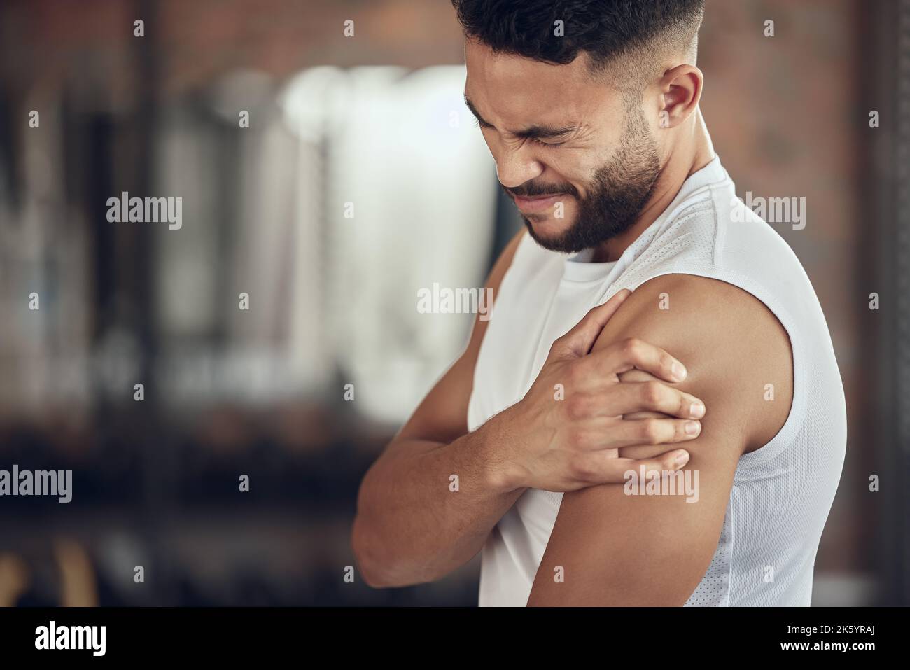Young man with shoulder pain in the gym. Fit athlete touching his arm in pain. Active ...