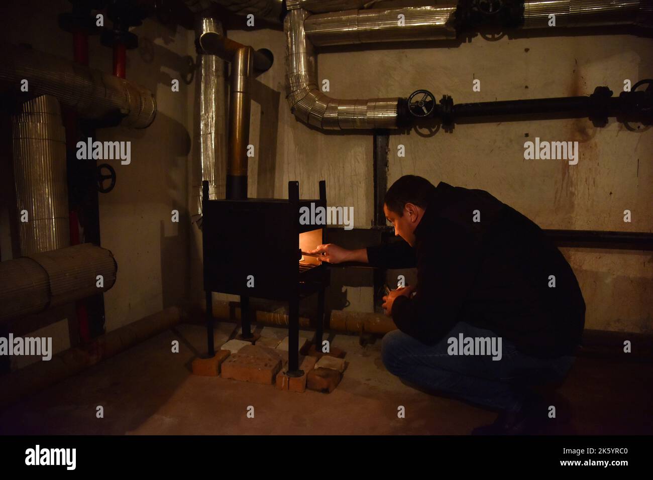 A man lights a metal stove in the basement of a house that serves as a ...