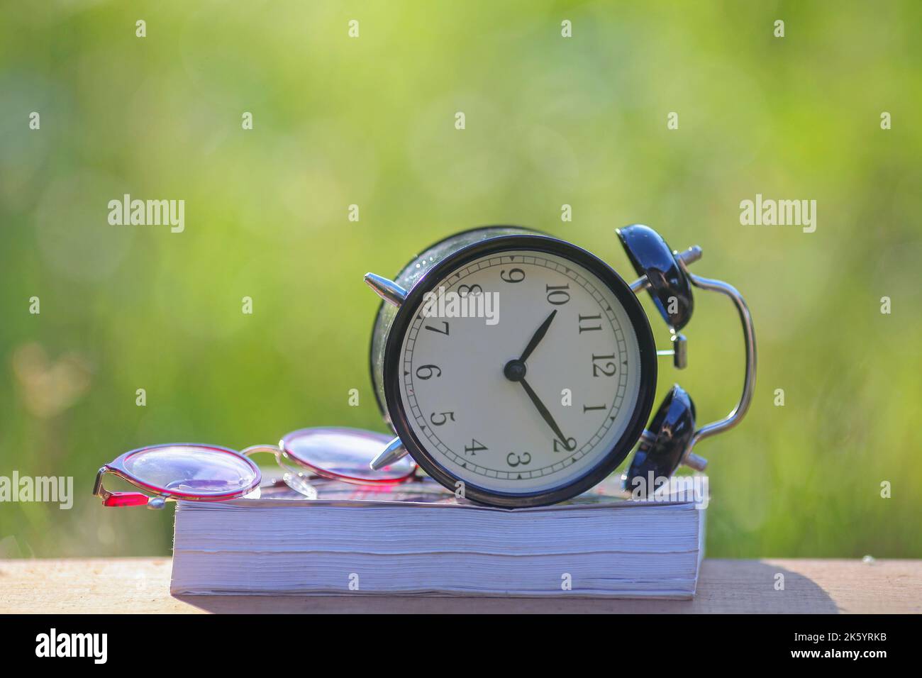 Black alarm clock stacked on old dictionary with pink flower and ...
