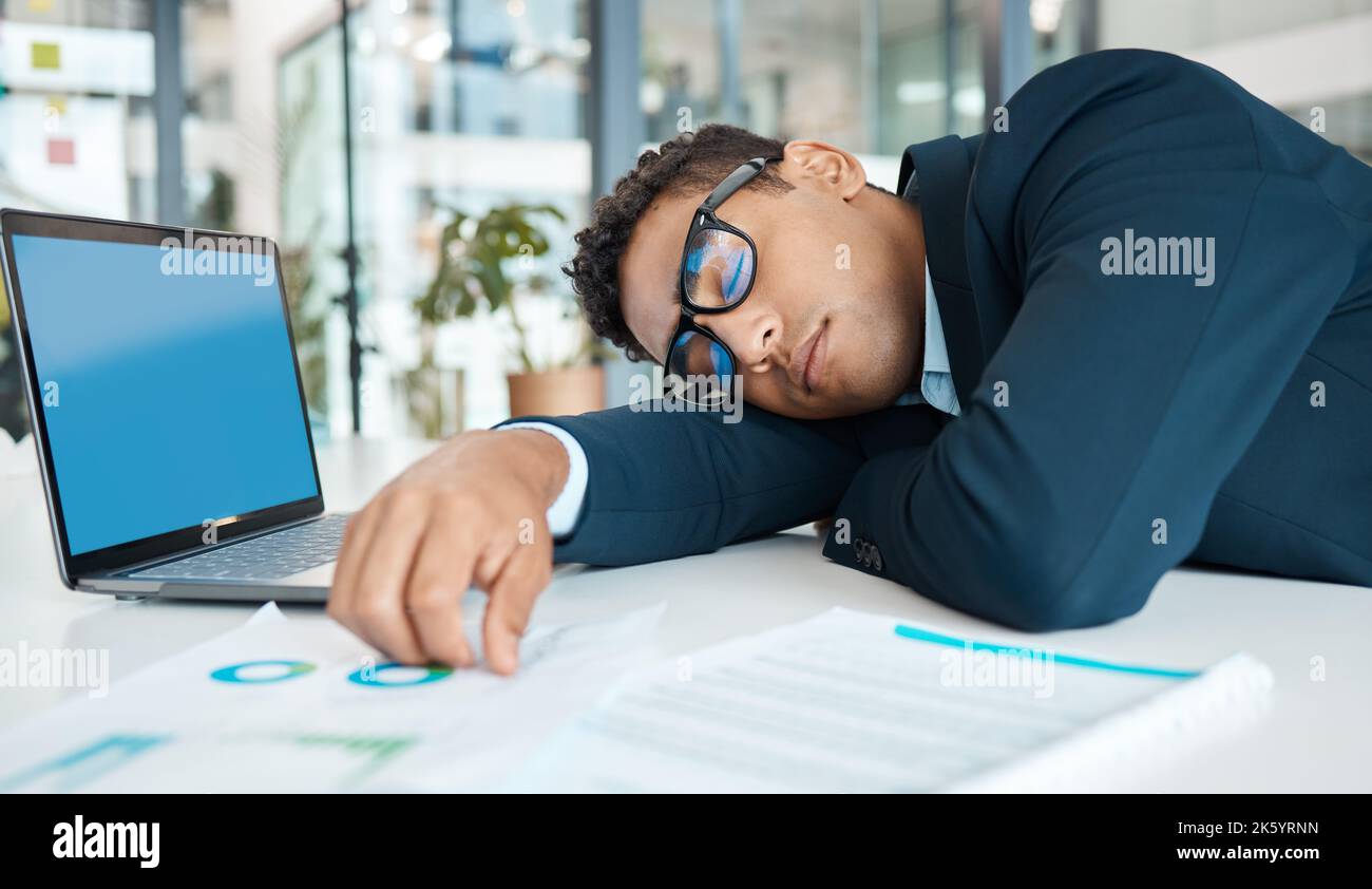 Young mixed race businessman napping and working on a laptop at a table ...