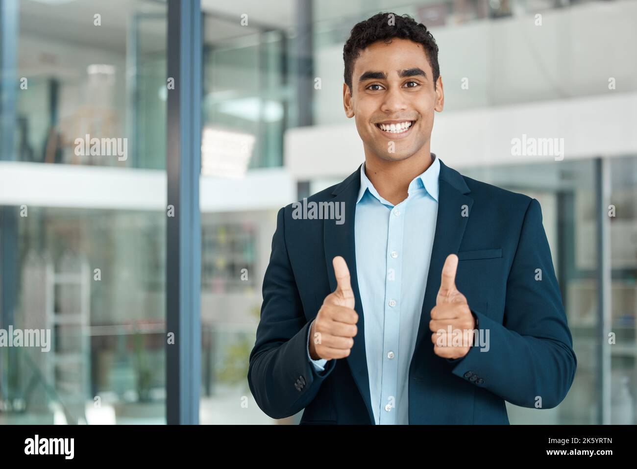 Young happy mixed race businessman showing two thumbs up standing alone ...