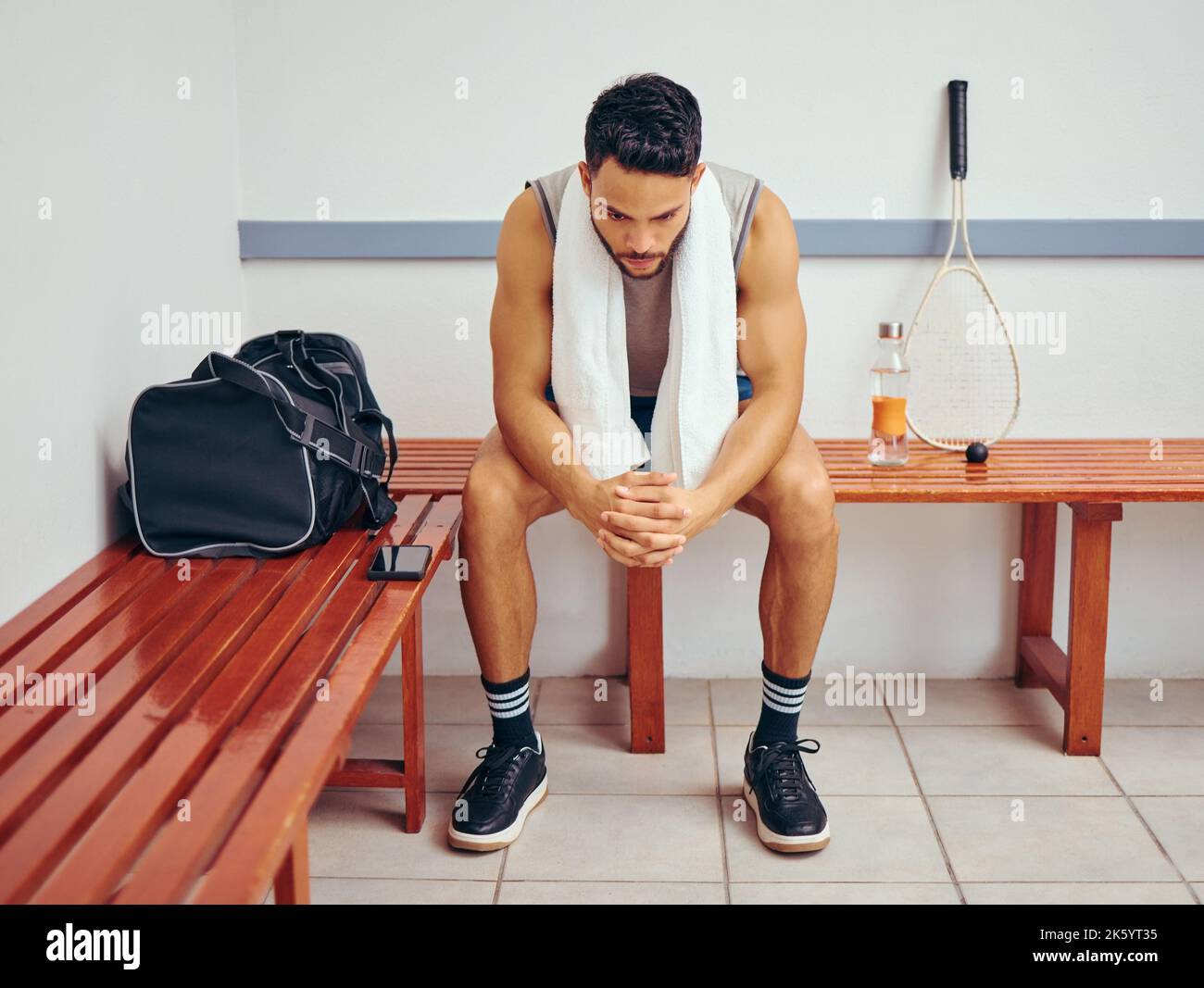 Young player sitting on a bench in his locker room. Serious mixed race ...