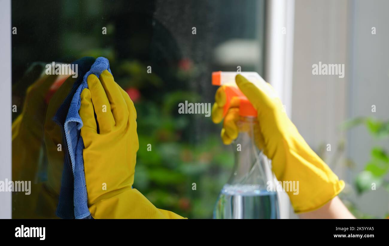 Female hands cleaning window outside using detergent spray and rag ...
