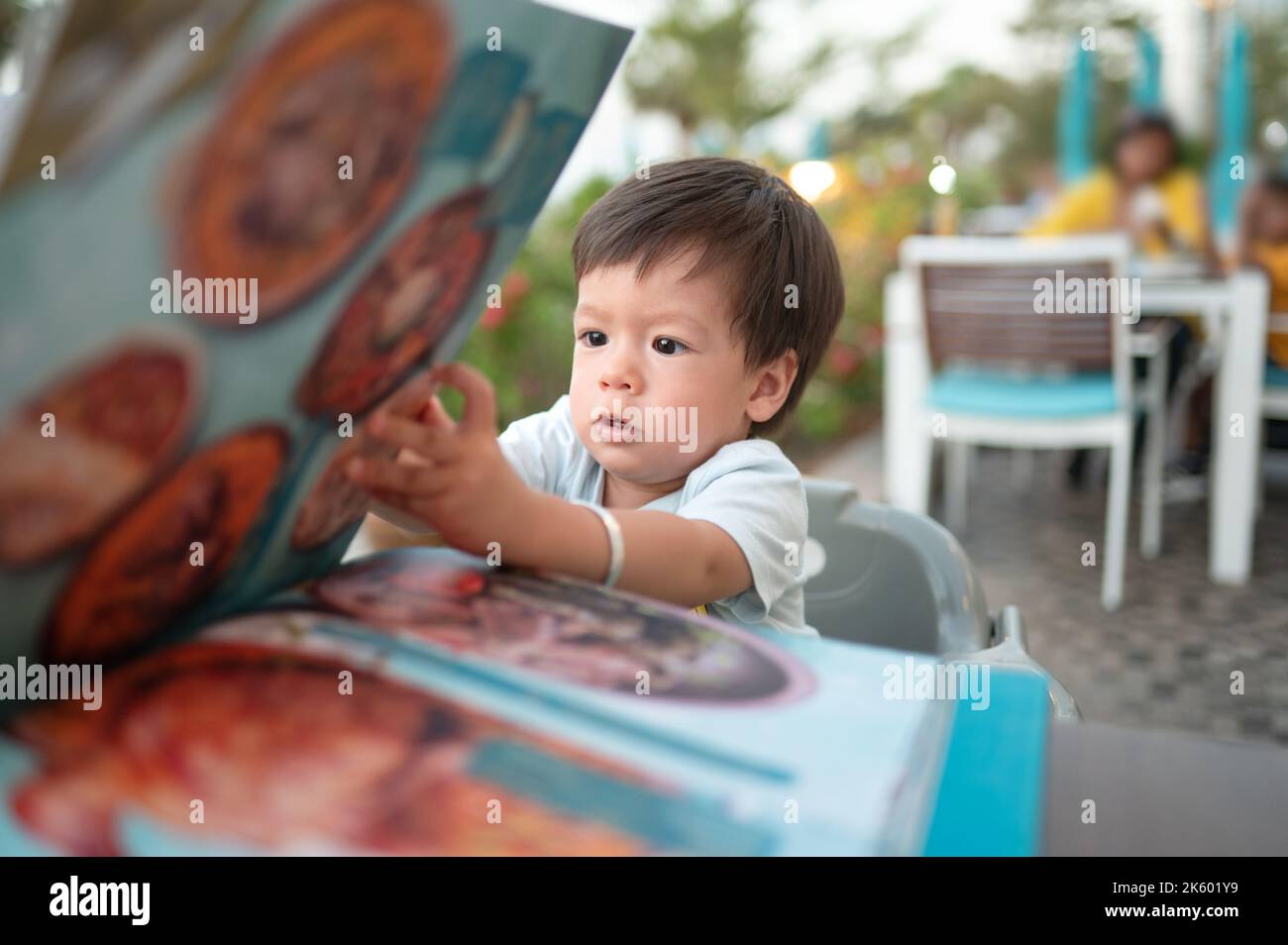 Handsome mixed race one year old baby boy looking at the menu to choose ...