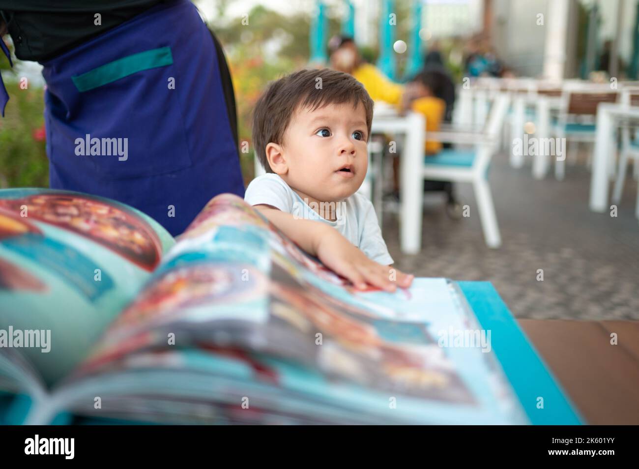Handsome mixed race one year old baby boy looking at the menu to choose ...