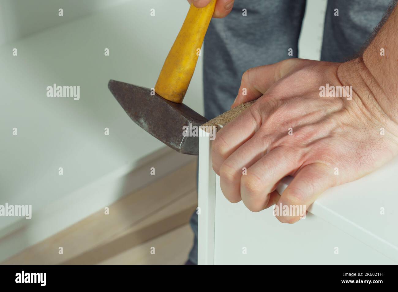Male hands hold metal hammer with yellow plastic handle, driving dowel ...