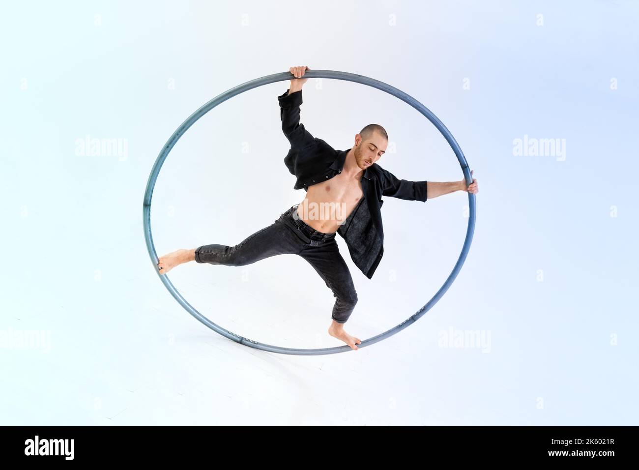 Full body barefoot man in jeans and black shirt doing trick on cyr ...