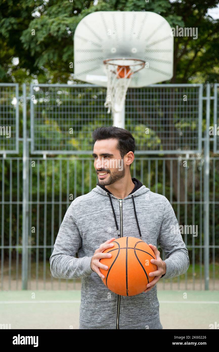 Smiling handsome man holding a basketball ball outdoors in a basketball ...