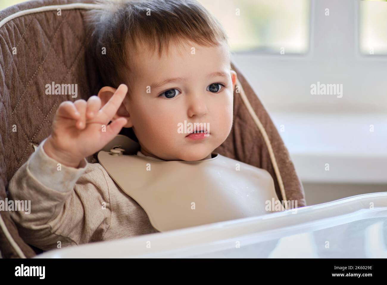 A thoughtful toddler baby sits at an empty table without food. A child ...
