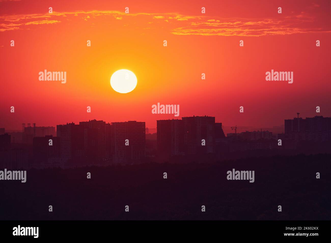 A big red sun in the sunset sky over the roofs of buildings, urban ...