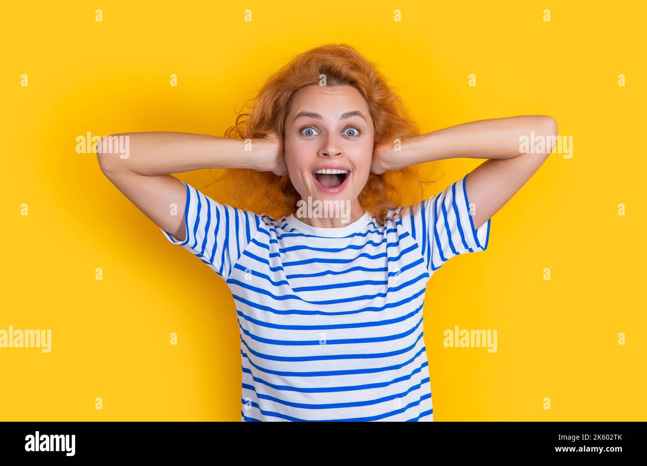 surprised redhead girl hear loud noisy sound isolated on yellow ...