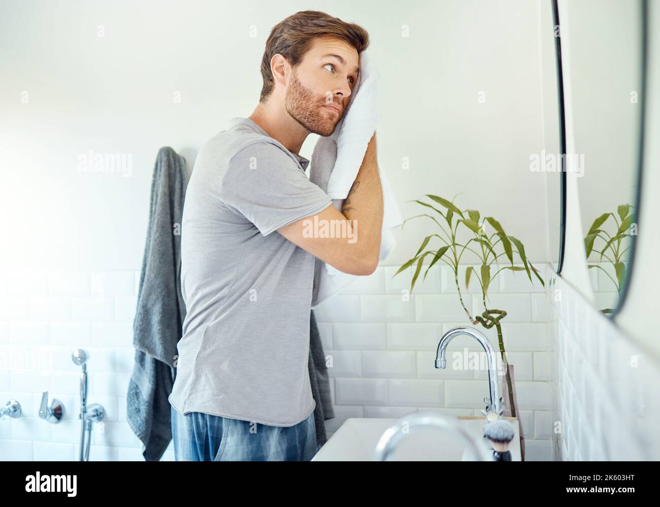 One handsome man washing his face in a bathroom at home. Caucasian male using a towel to dry his ...