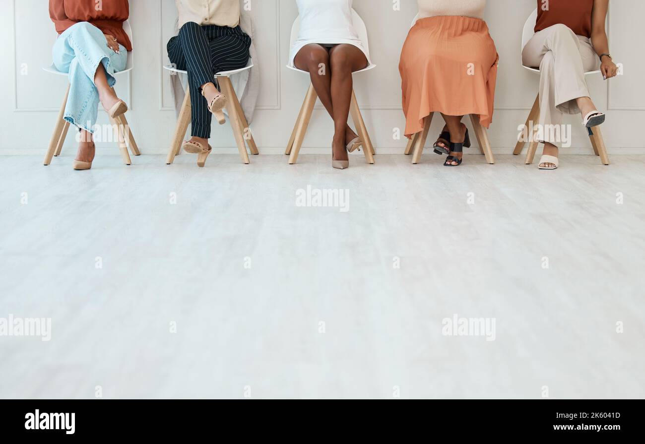 Group of five businesswomen sitting on chairs against a wall in an ...