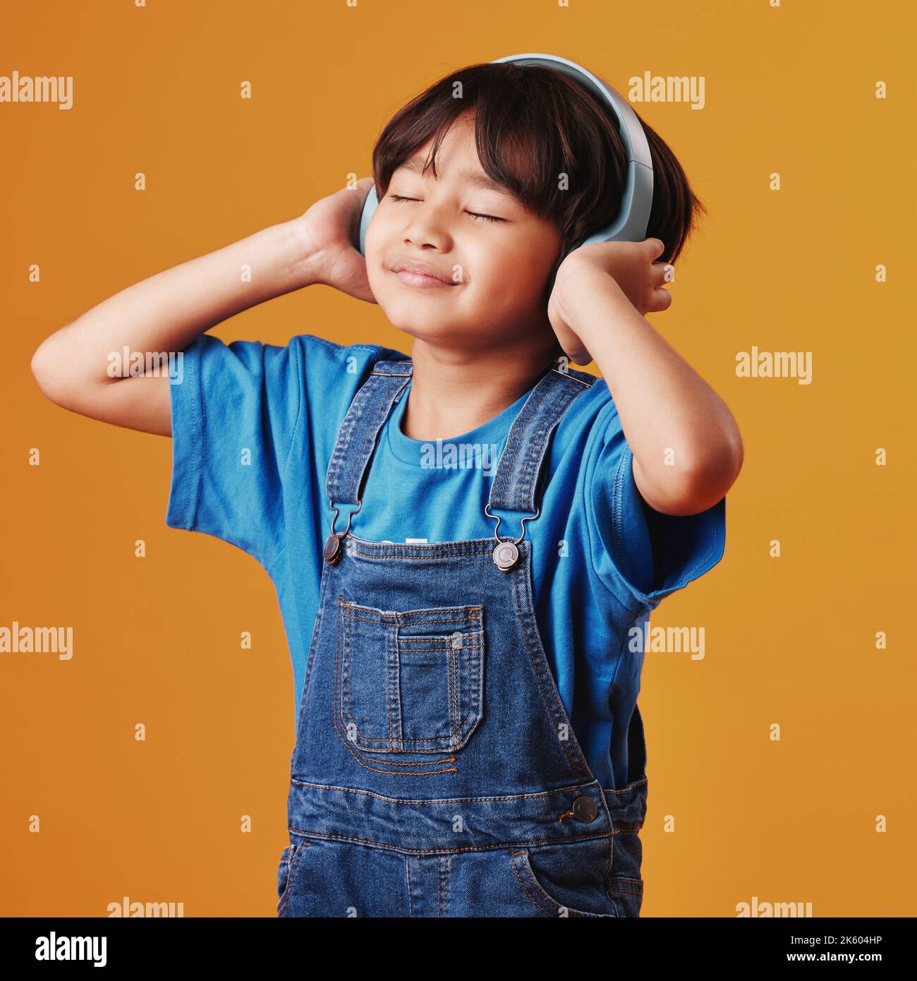 A cute little asian boy enjoying listening to music while wearing headphones against an orange ...