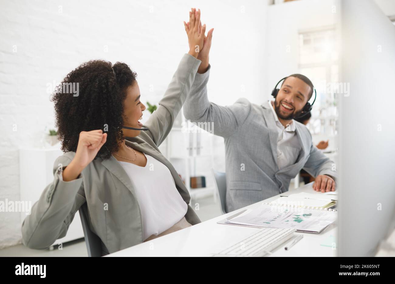 Two young happy mixed race call center agents giving each other a high ...