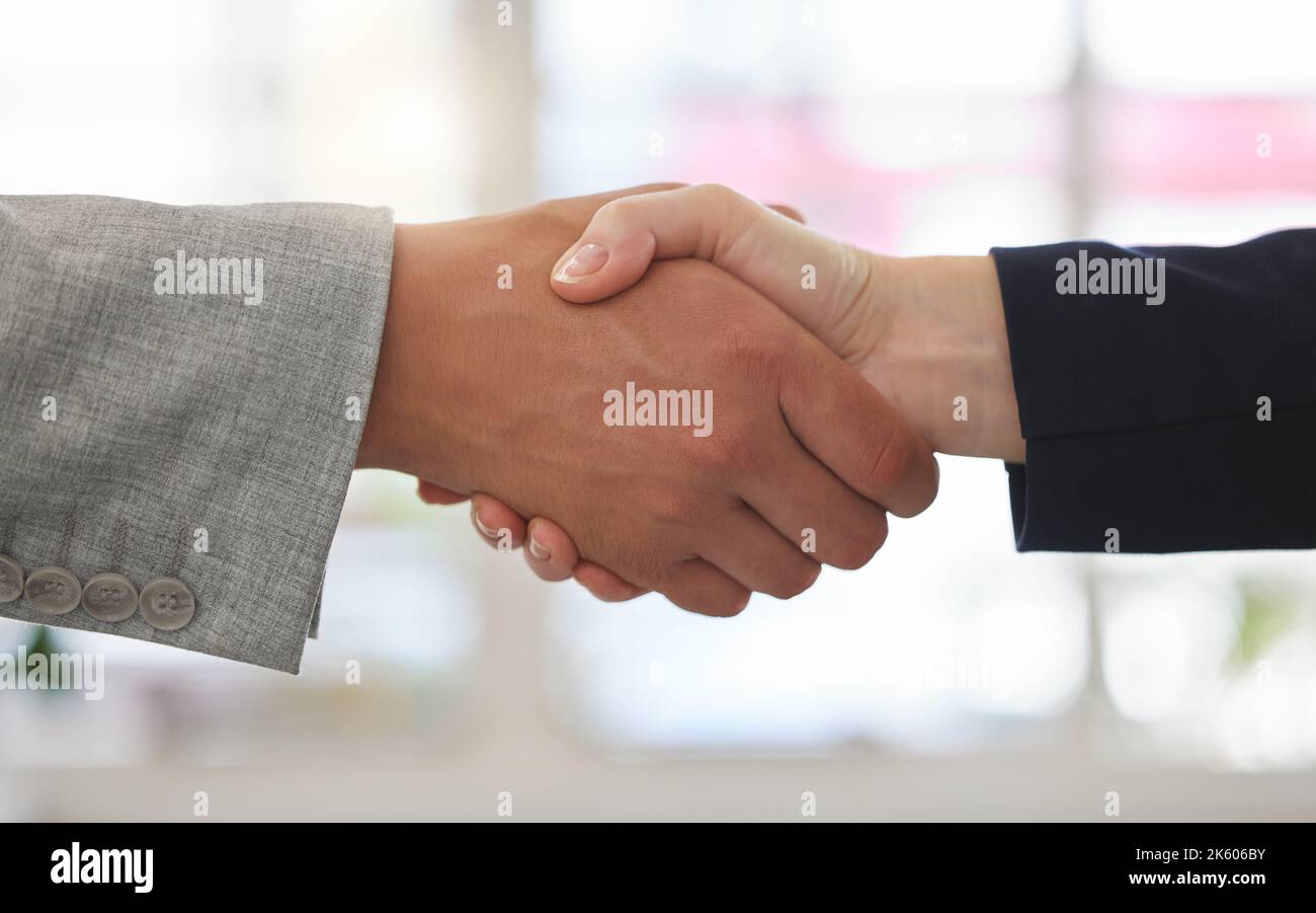 Two businesspeople shaking hands while in an office together at work ...
