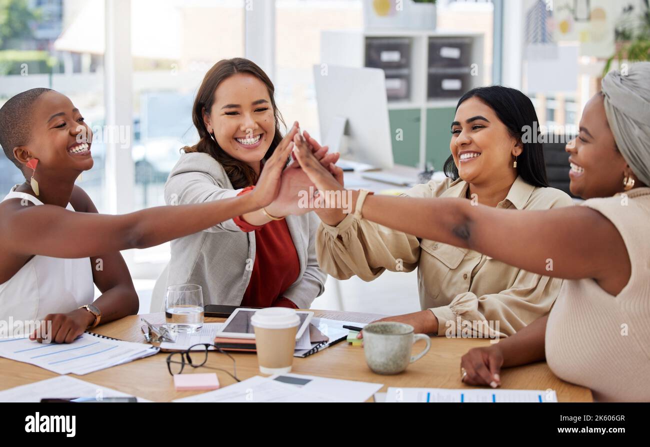 Diverse group of smiling ethnic business women giving high five after brainstorm meeting in ...