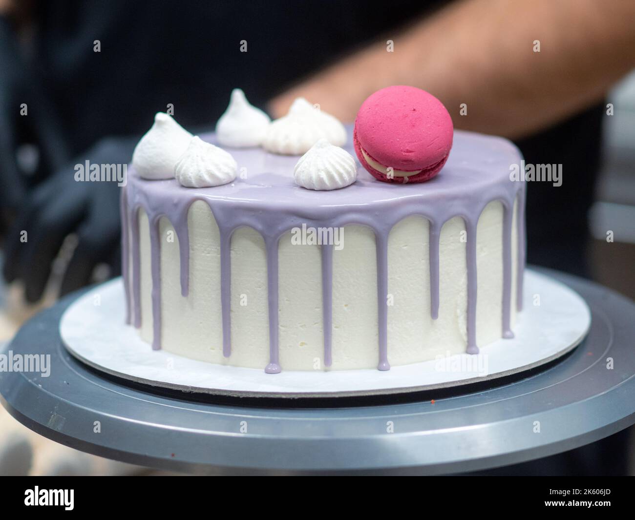 frosted drip cake on stand while designer works on topping Stock Photo ...