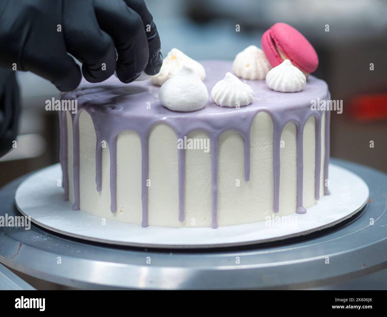 frosted drip cake on stand while designer works on topping Stock Photo ...
