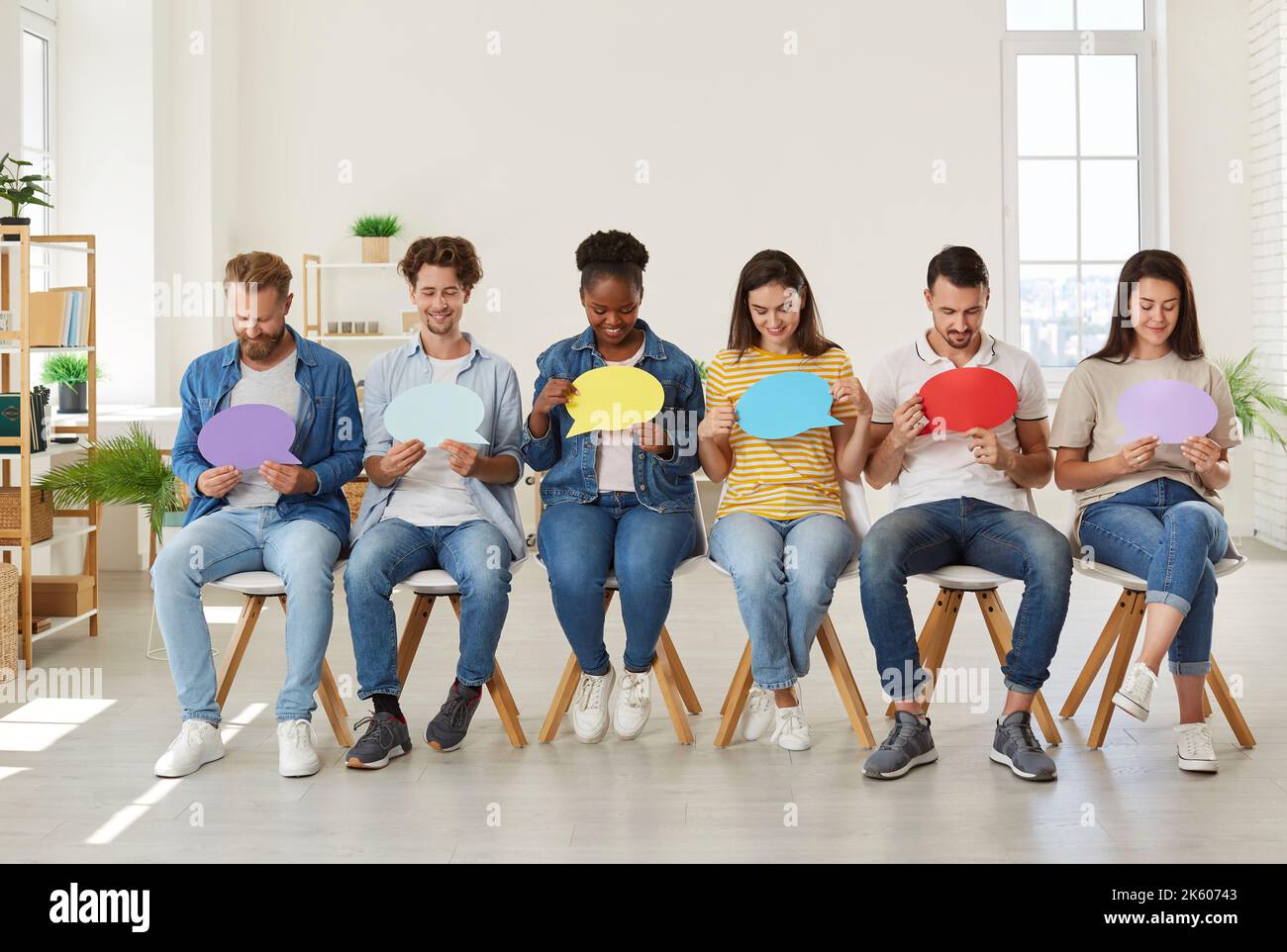 Group of happy diverse people sitting in row and holding colorful ...