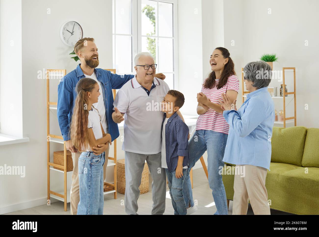A big cheerful family is standing in the room next to grandpa hugging ...