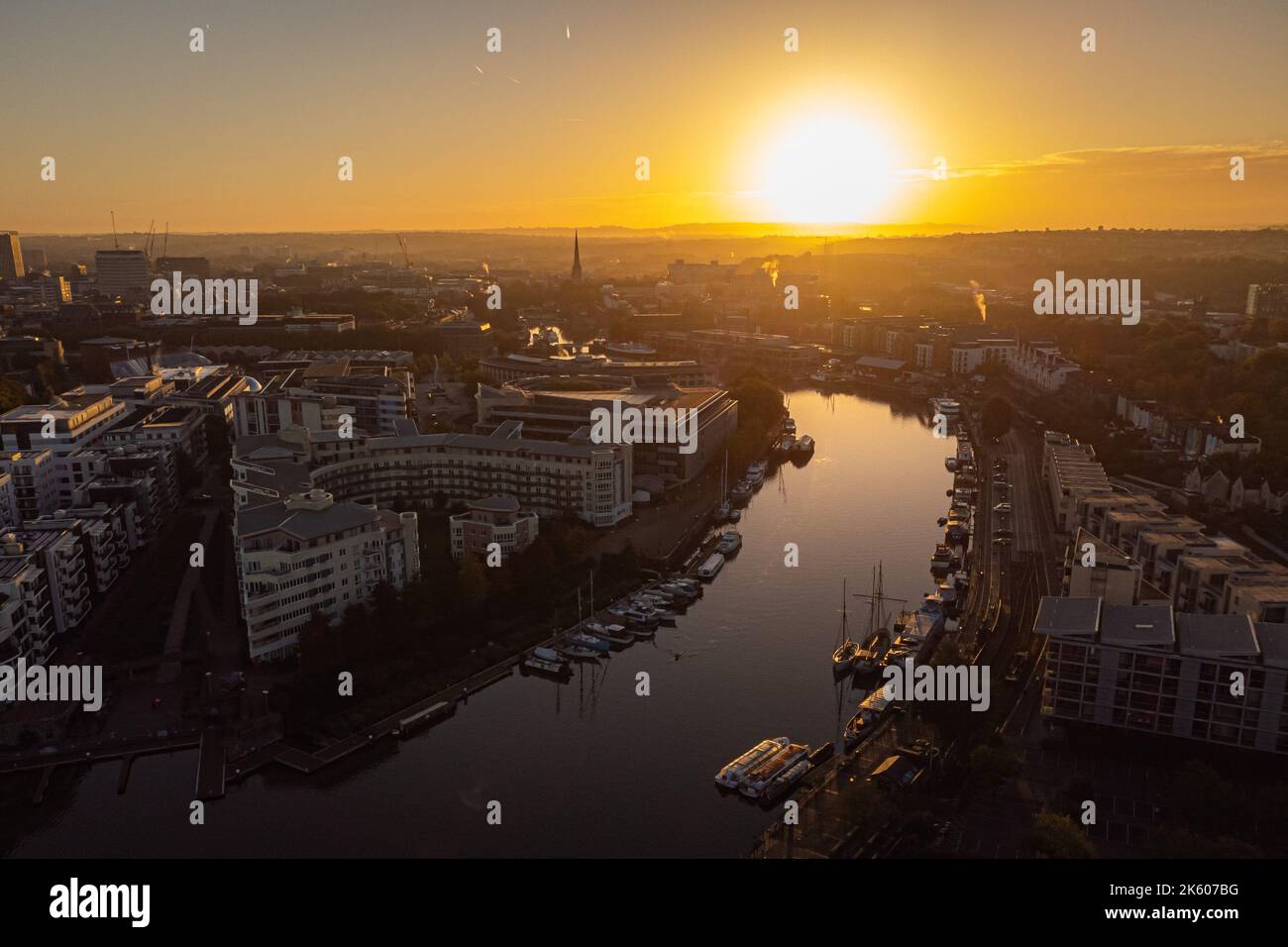The rising sun strikes buildings and the water at Bristol Harbourside ...