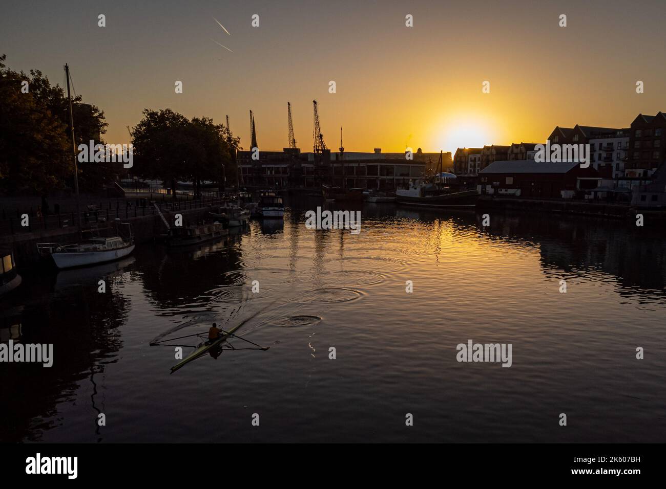 The rising sun strikes buildings and the water at Bristol Harbourside ...